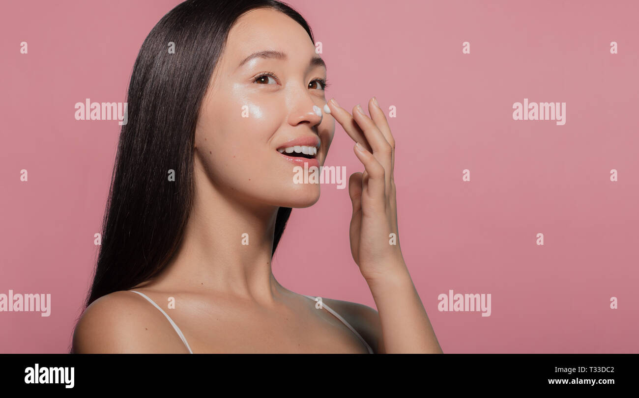 Close up of a youthful female model applying moisturizer to her face ...