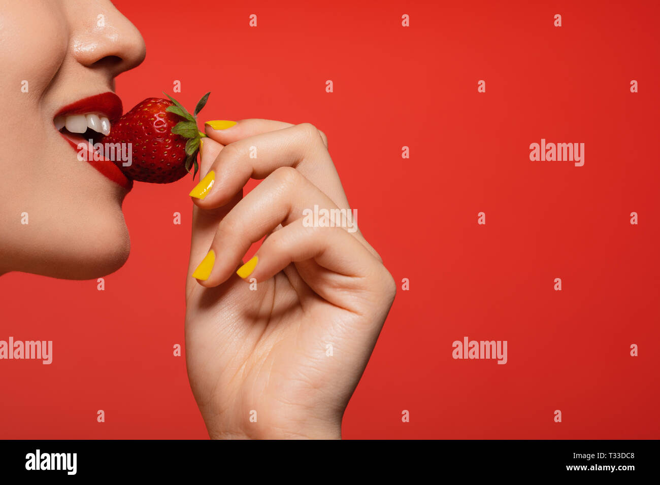 Studio shot of a beautiful young woman eating a strawberry against red ...