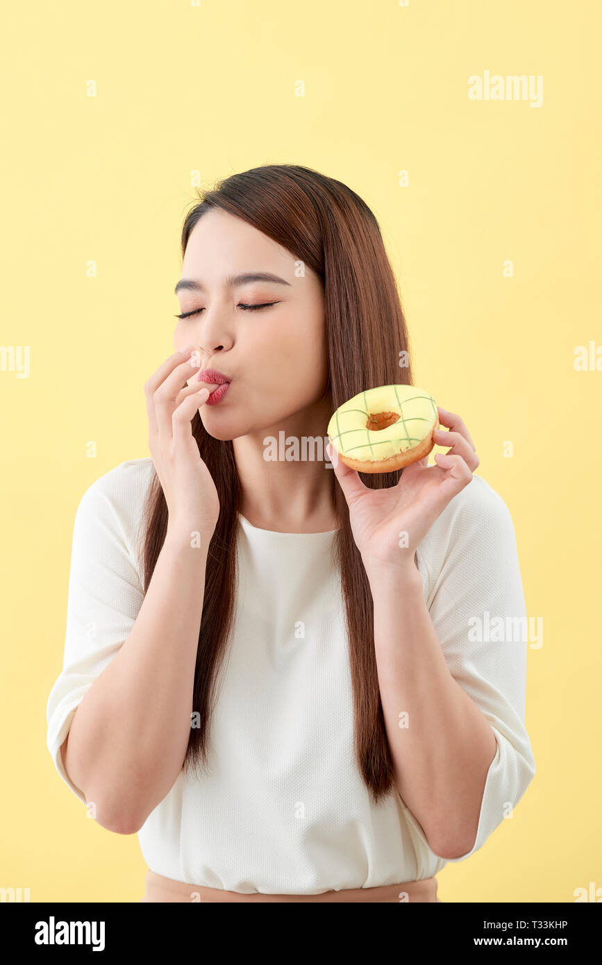 Portrait of a lovely young asian woman eating donuts isolated over ...