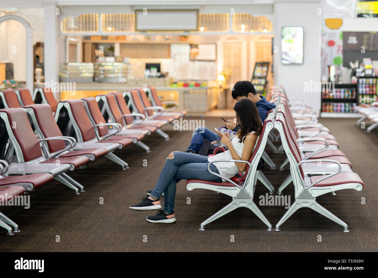 Unidentified couple using cell phone while sitting on chair in lounge ...