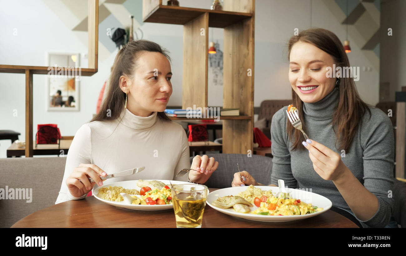 Two woman friends are eating together in cafe and talking, enjoying ...