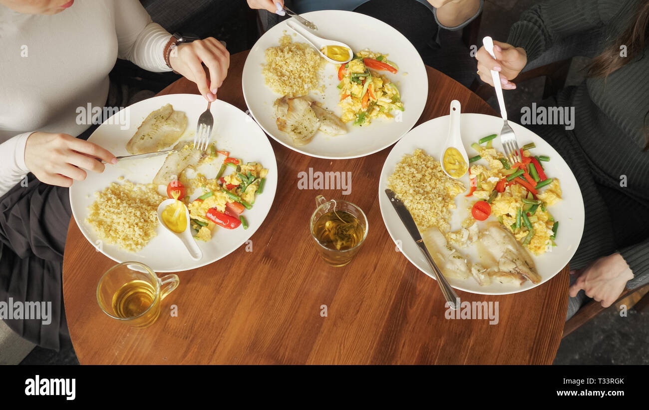 Three women friends are eating their food in cafe. Plates on the table ...