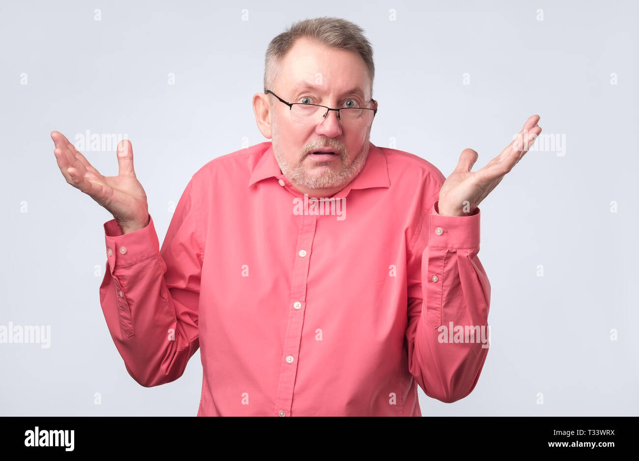 Doubtful senior man in red shirt gesturing with hands in doubt and ...