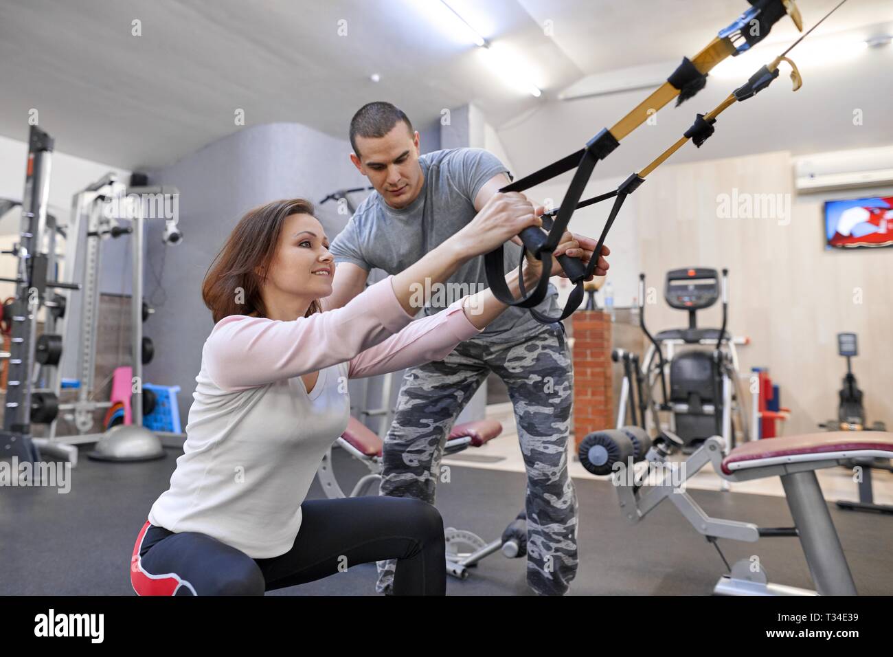 Mature woman exercising in gym using fitness straps loops. Male ...