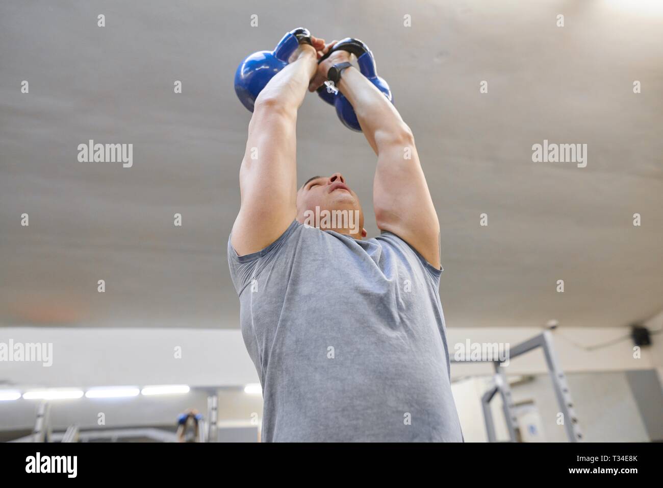 Strong muscular athlete man exercising with kettlebells in gym, weight ...