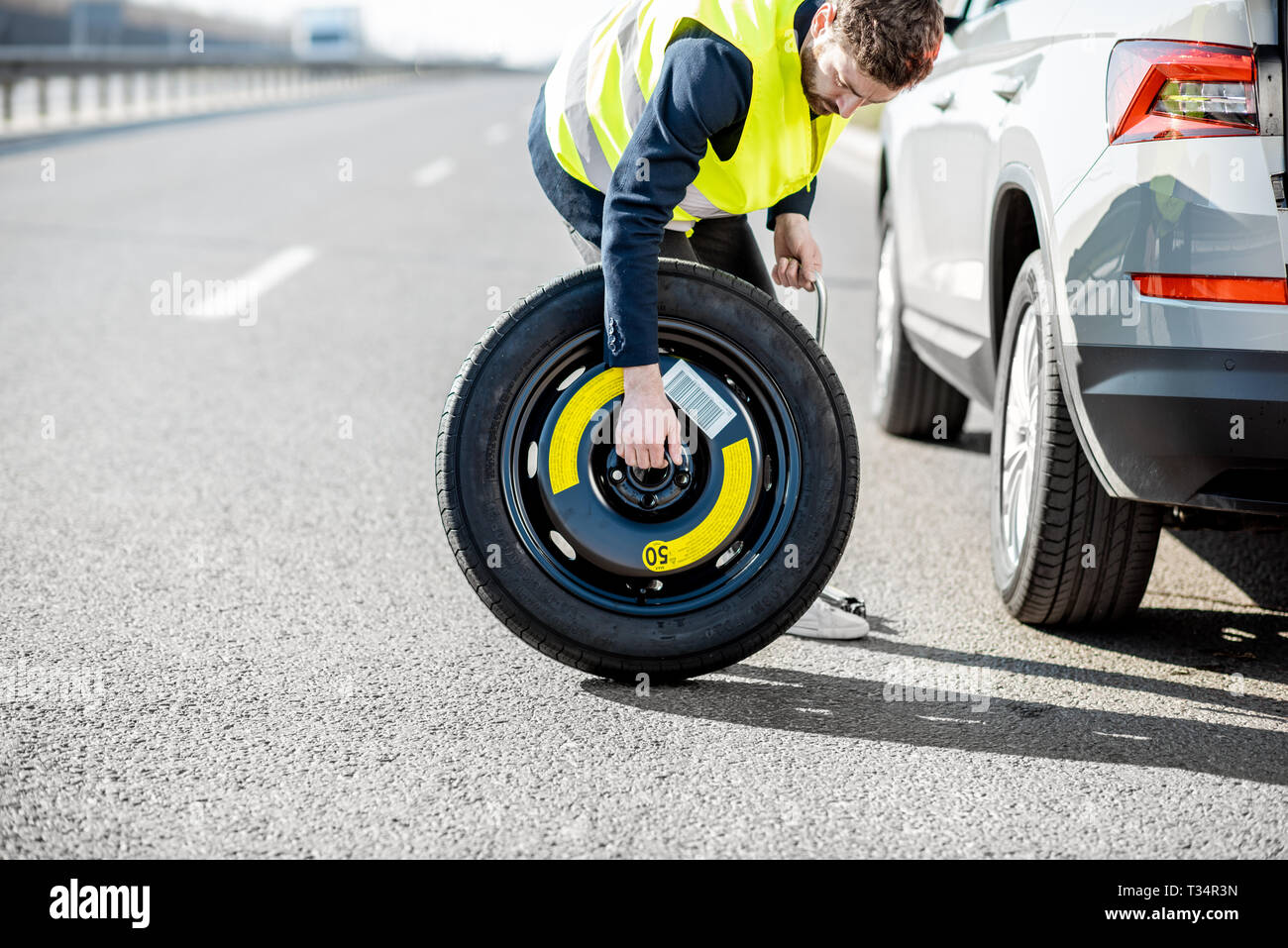 Man changing wheel standing with spare wheel near the broken car on the ...