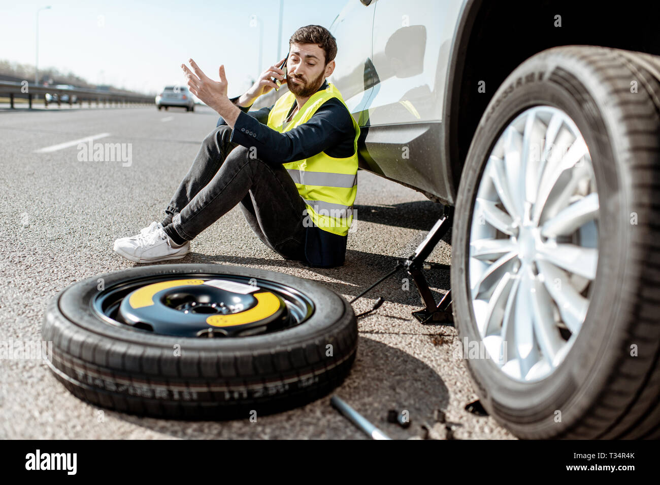 Man calling the road assistance sitting near the car with broken wheel ...