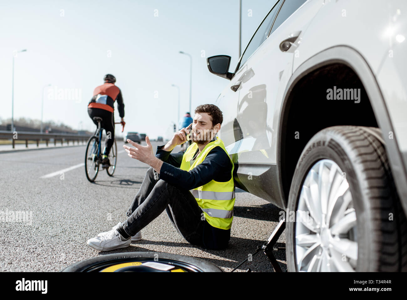 Man calling the road assistance sitting near the car with broken wheel ...