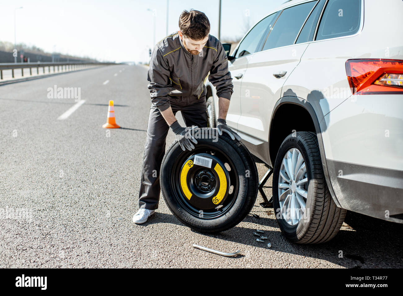 Road assistance worker in uniform changing car wheel on the highway ...