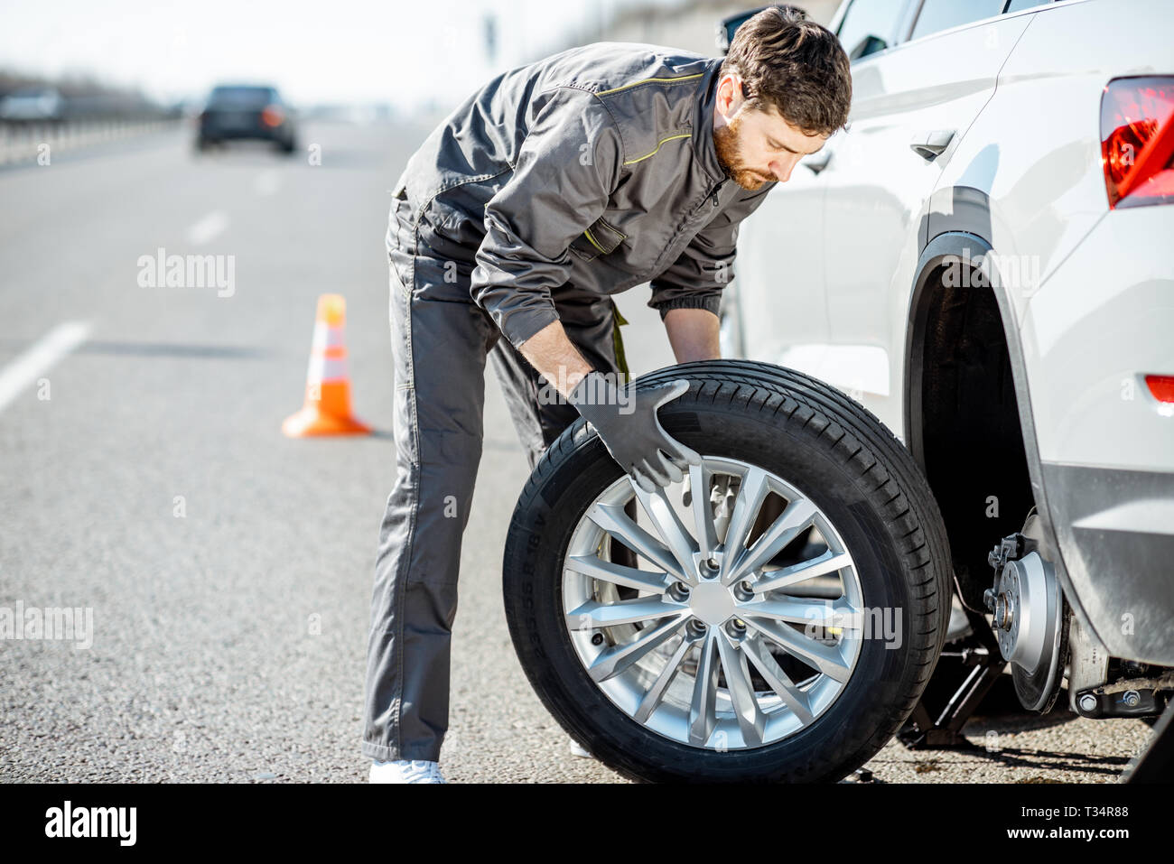 Handsome road assistance worker in uniform changing car wheel on the ...