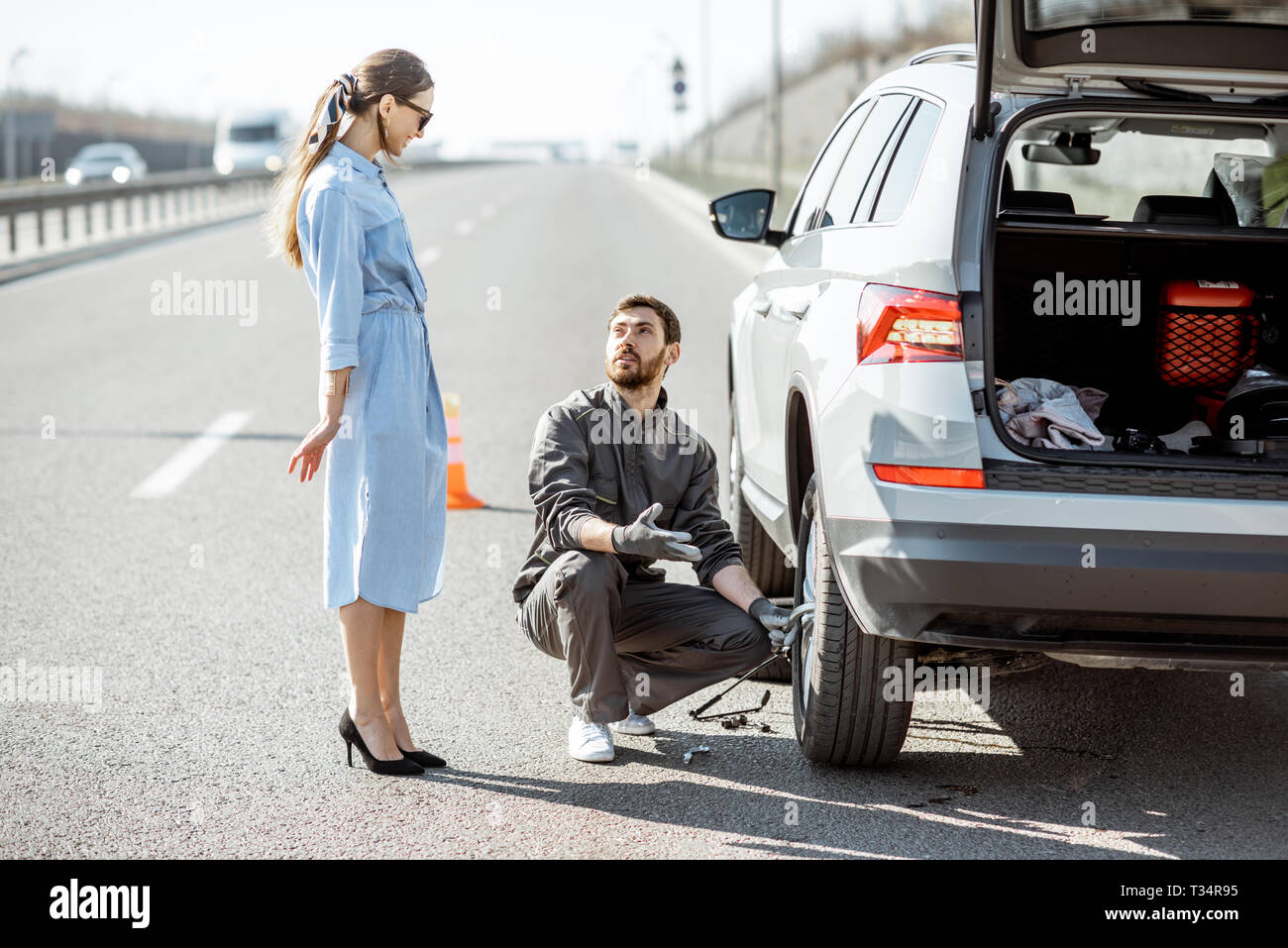 Road assistance worker helping young woman to change a car wheel on the ...