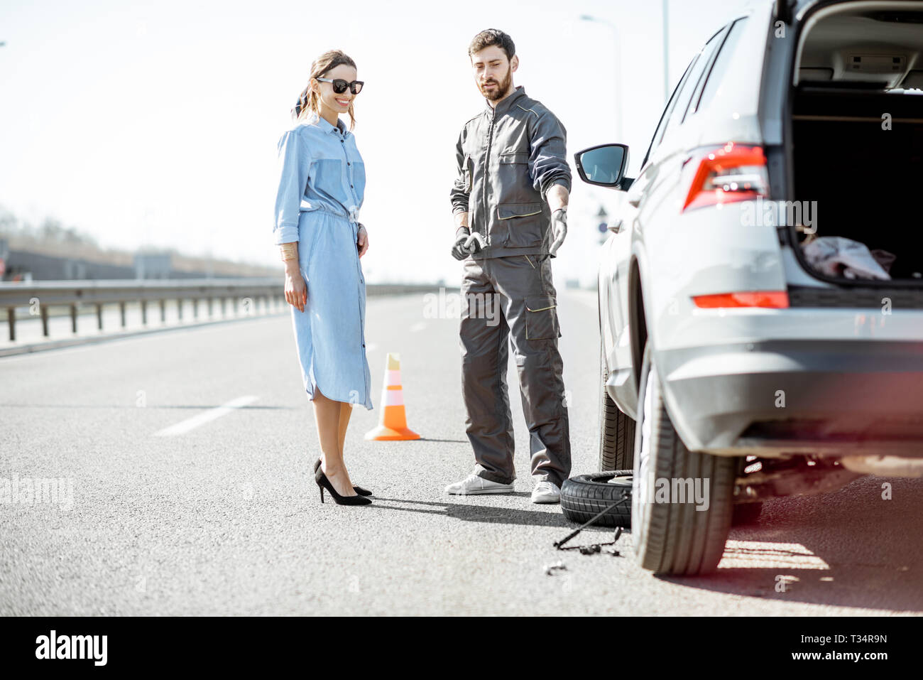 Road assistance worker in uniform with young woman standing near the ...