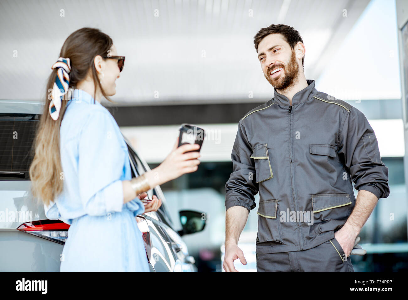 Smiling gas station worker in uniform talking with woman client at the ...