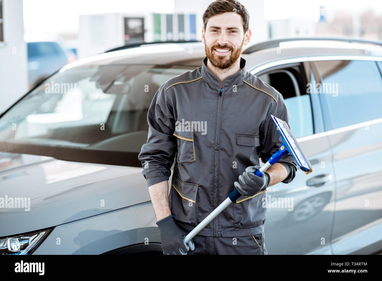 Portrait of a happy gas station worker in uniform with washing tool at ...