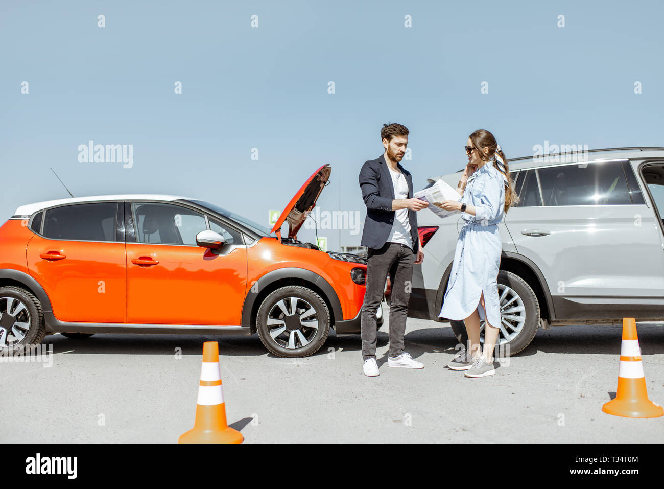 Man and woman arguing, standing together on the road with their cars on ...