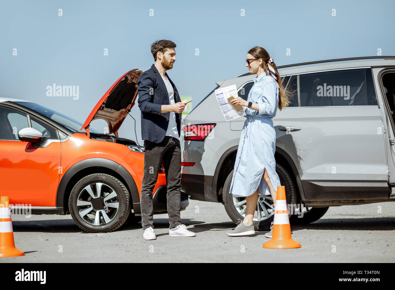 Man and woman arguing, standing together on the road with their cars on ...