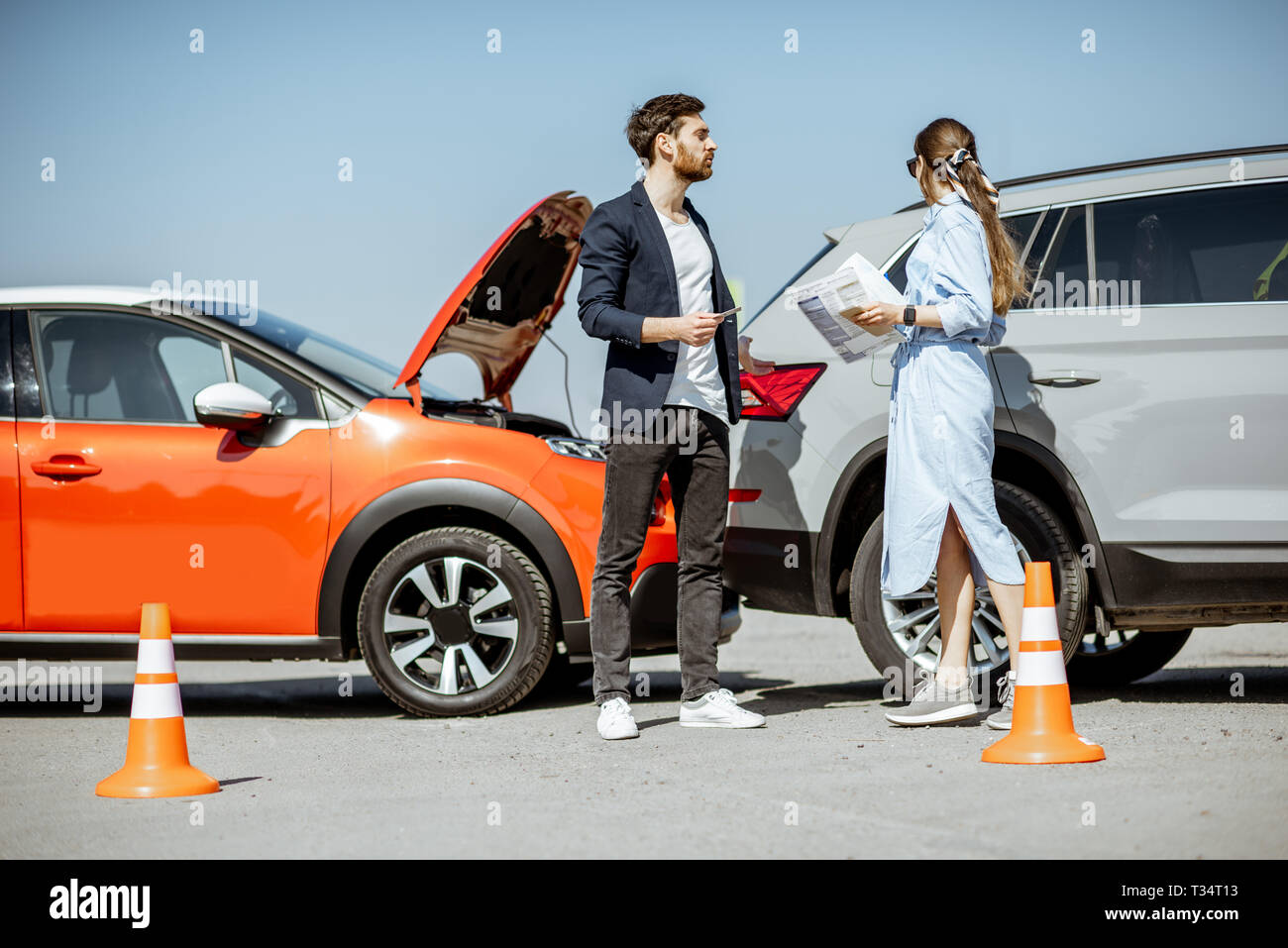 Man and woman arguing, standing together on the road with their cars on ...