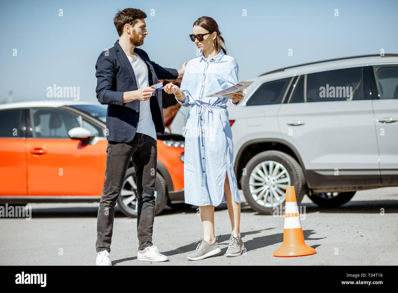 Man and woman arguing, standing together on the road with their cars on ...