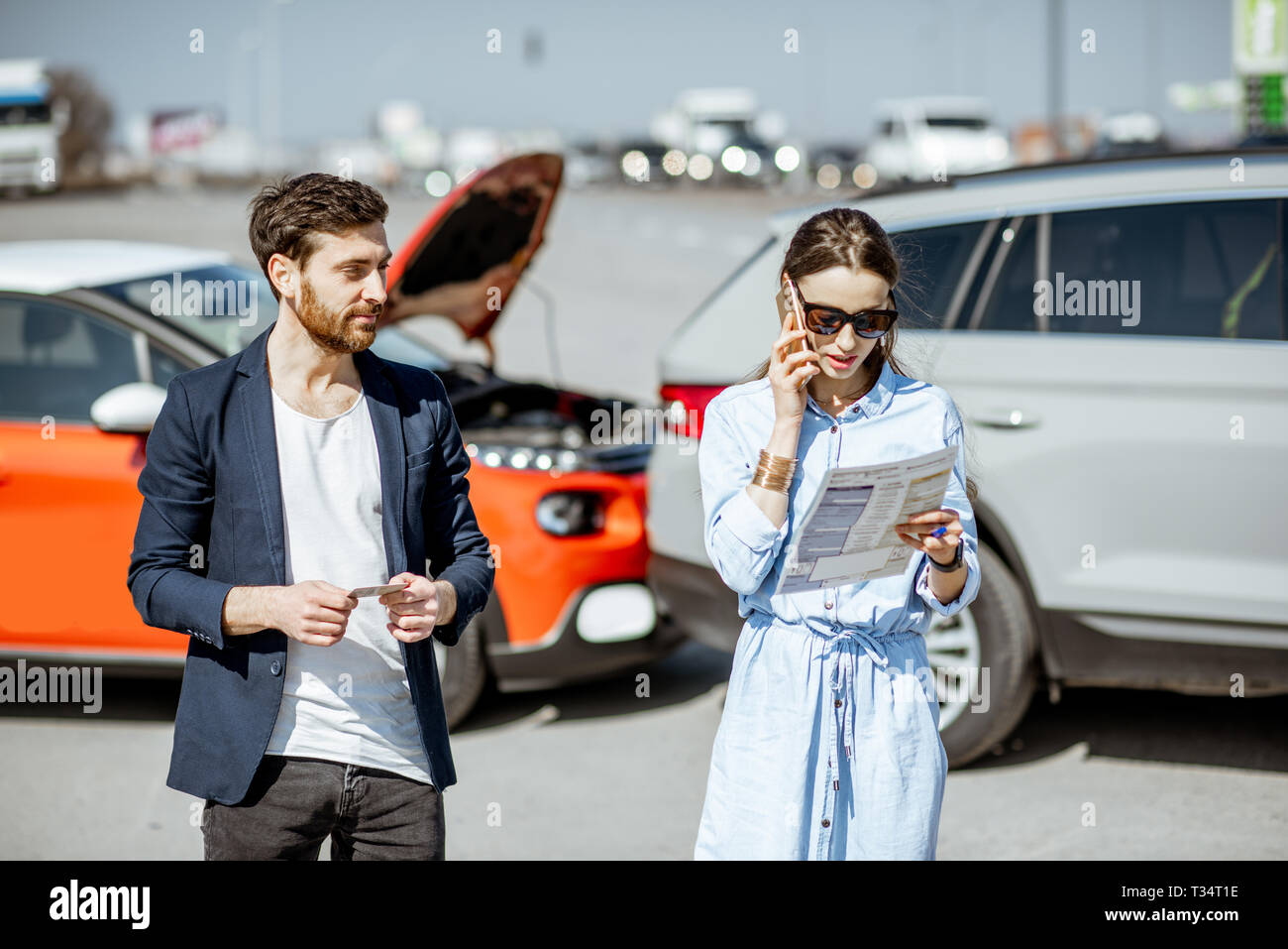 Man and woman arguing, standing together on the road with their cars on ...