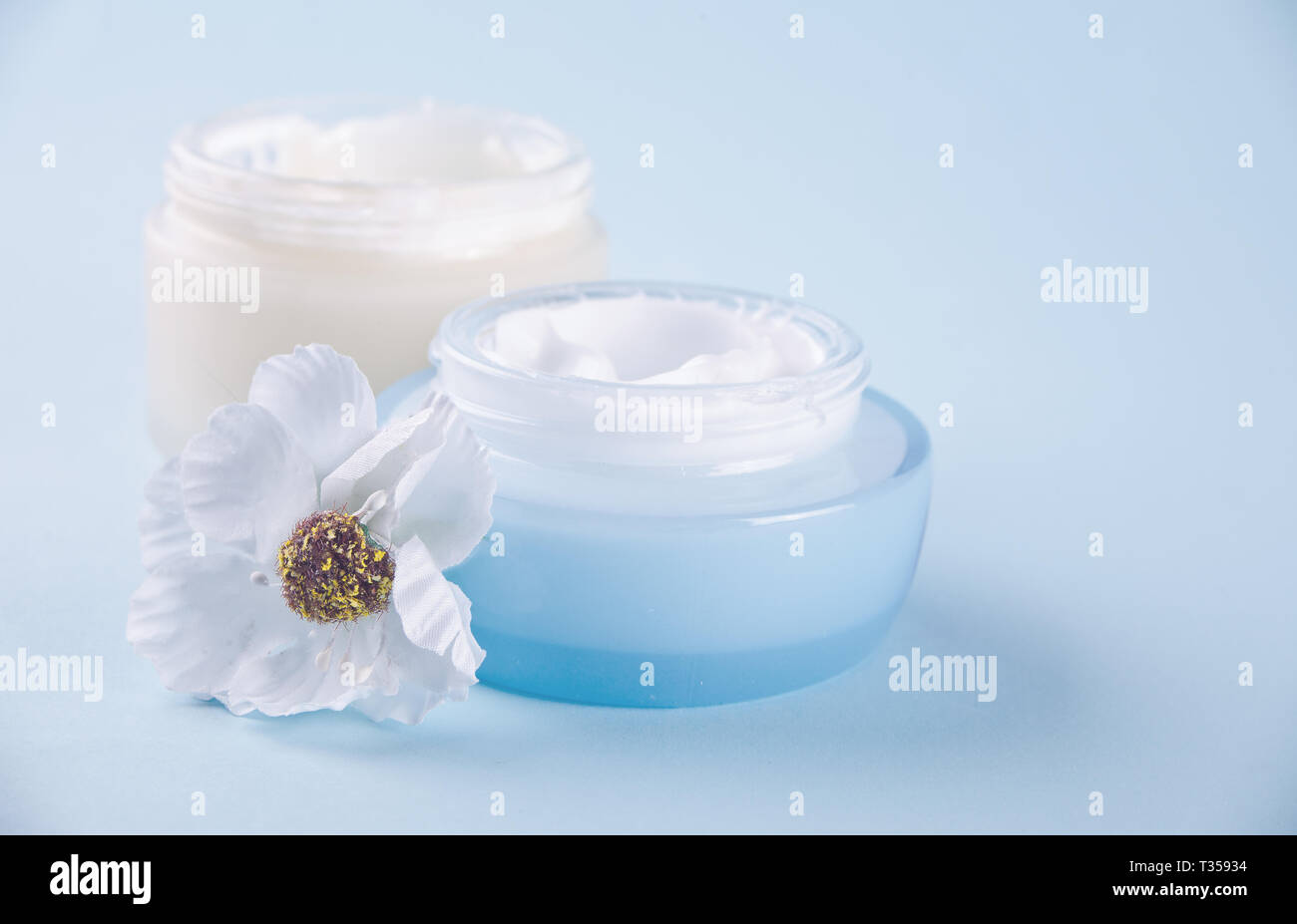 two glass jars of beauty cream with flower on the blue background Stock ...