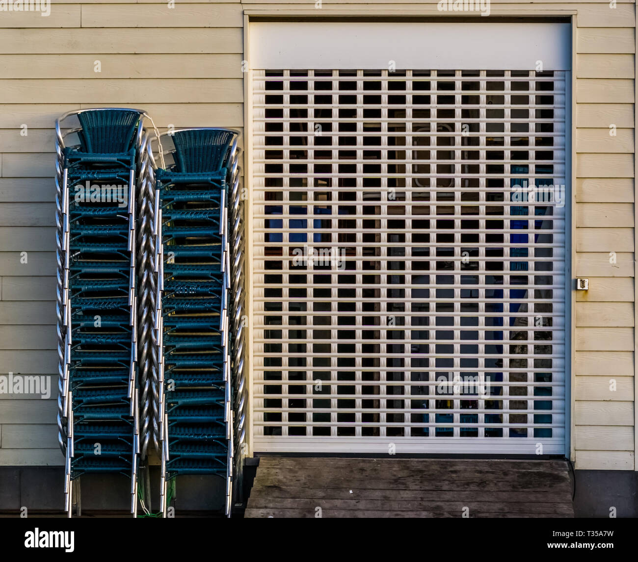 closed rolling shutter with stacked chairs next to it, closing time for ...