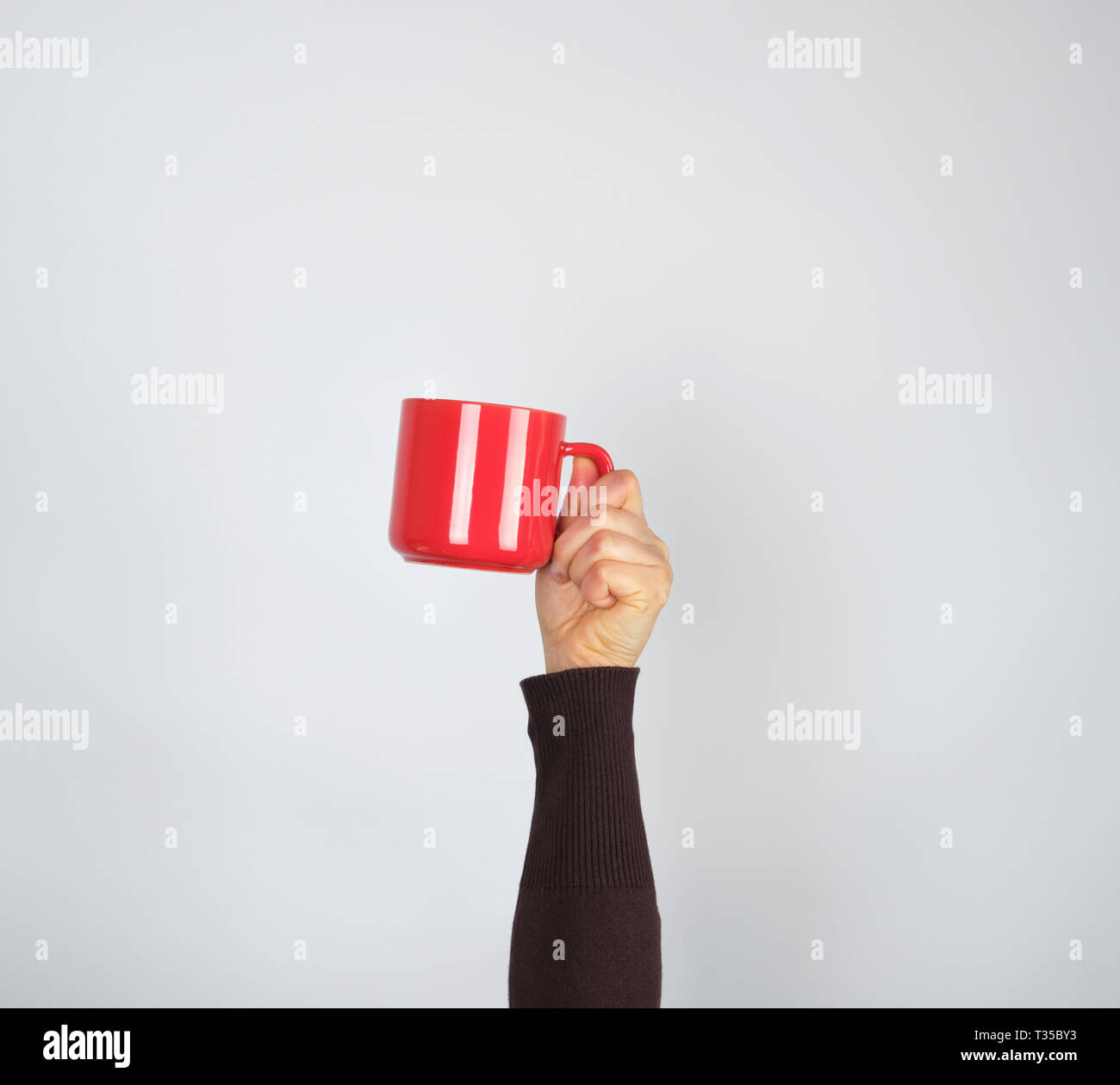 red ceramic cup in a female hand on a white background, hand is raised ...