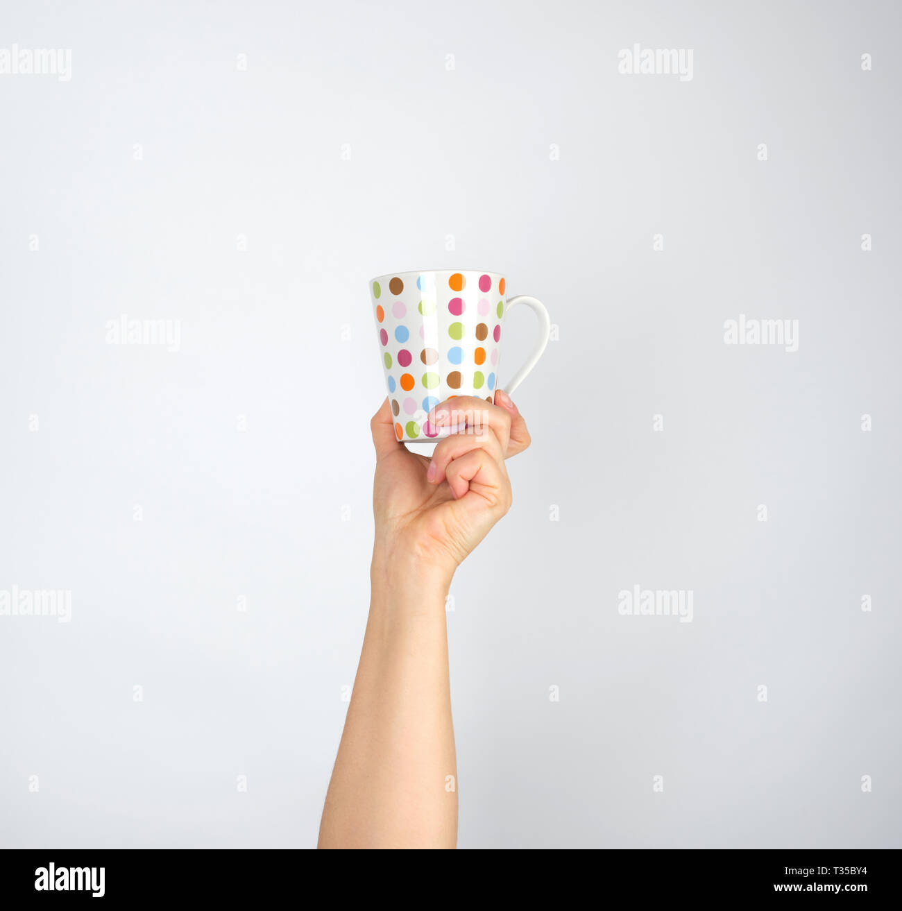 ceramic cup with multi-colored circles in a female hand on a white ...