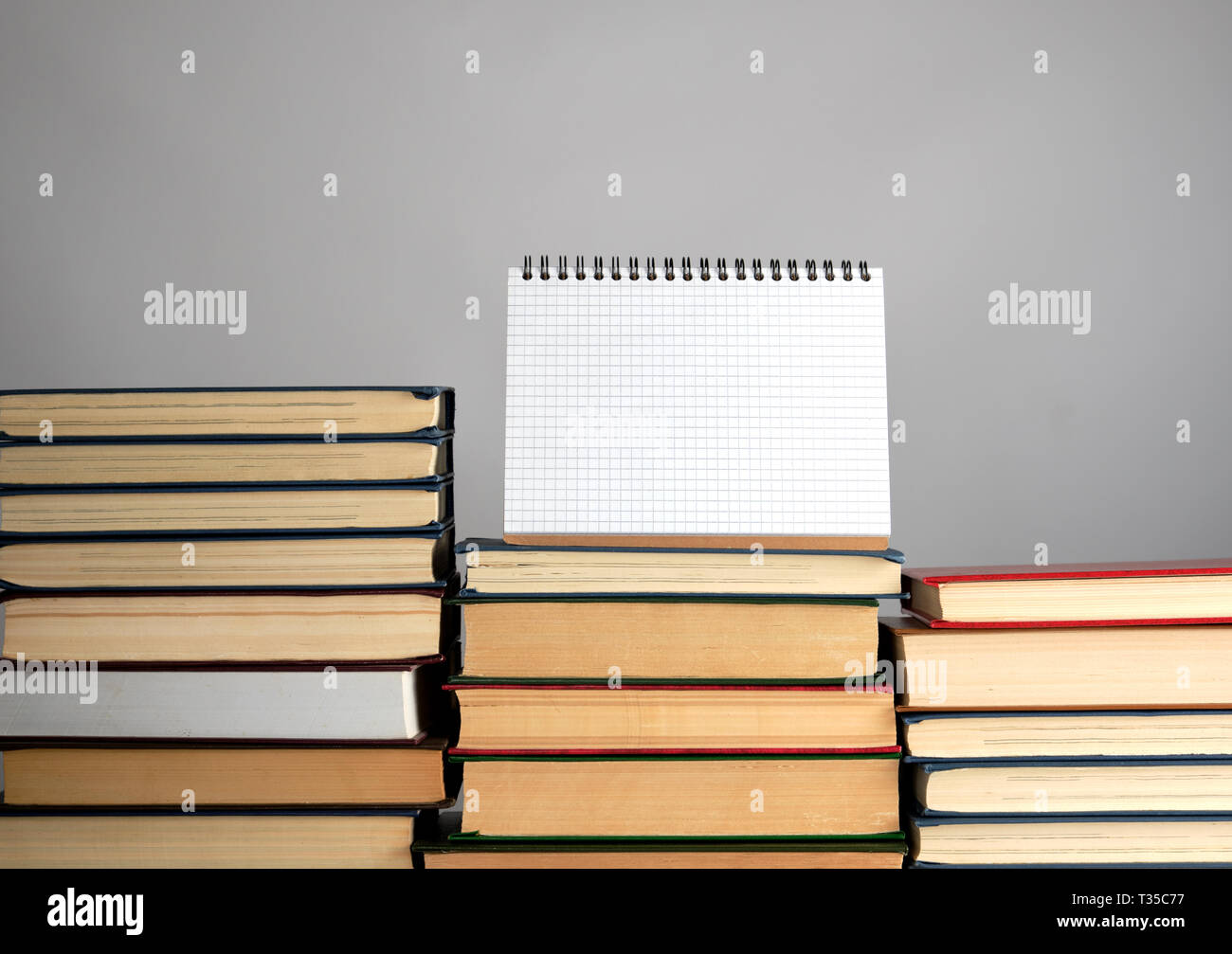 open blank notebook is standing on the stack of books, gray background ...