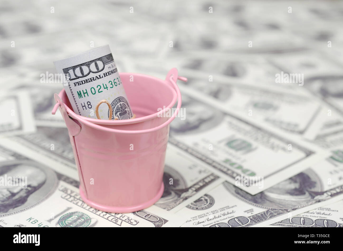 A bundle of US dollars in a metal pink pail on a set of dollar bills ...
