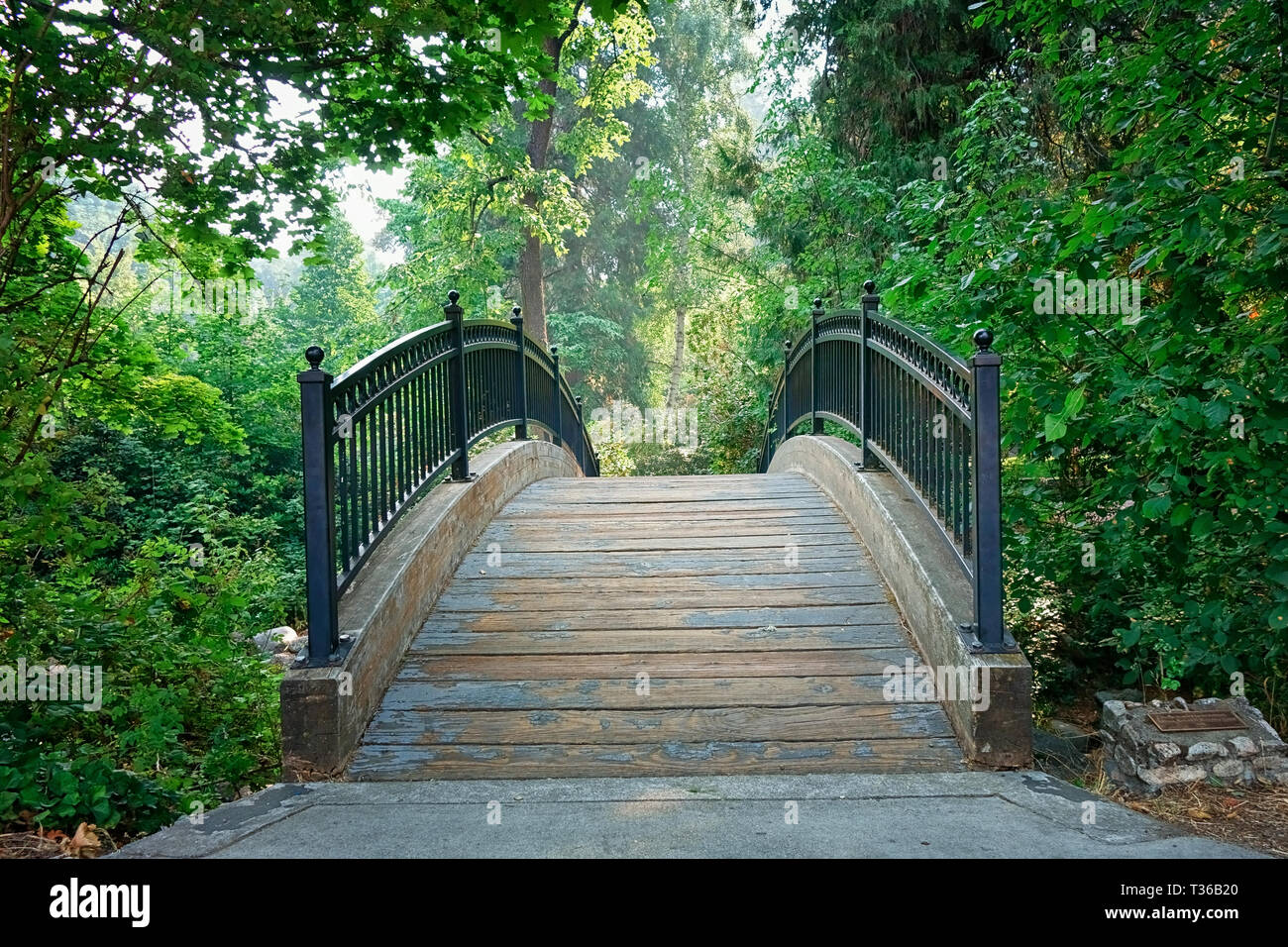 A wooden bridge with a wrought iron railing arching into the ...