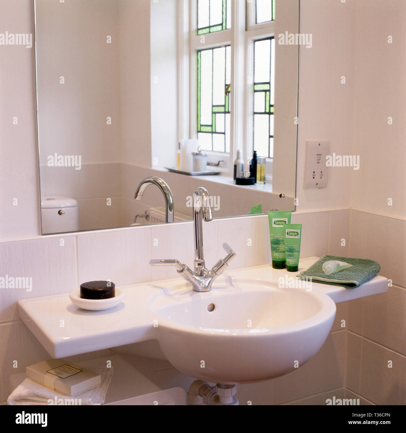 Mirror above basin with chrome tap in white bathroom Stock Photo - Alamy