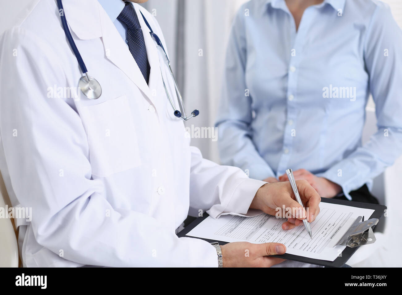 Male doctor holding application form while consulting female patient in ...