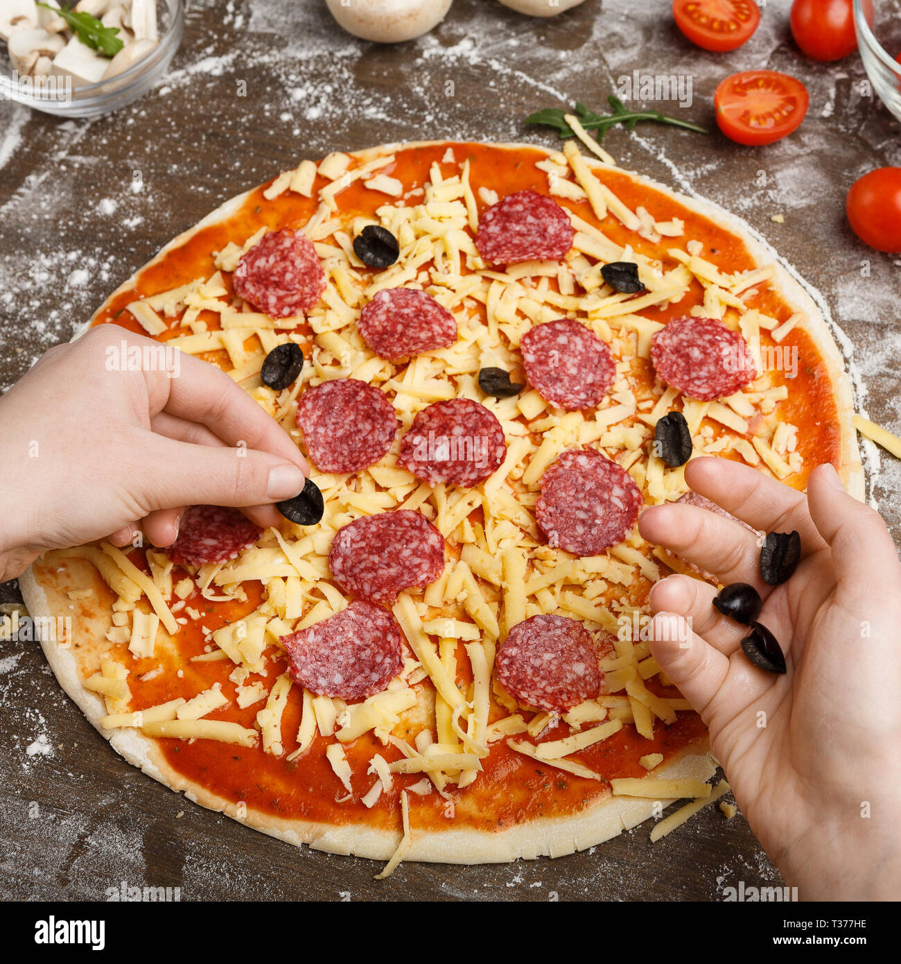Chef adding black olives to pizza, decorating it Stock Photo - Alamy