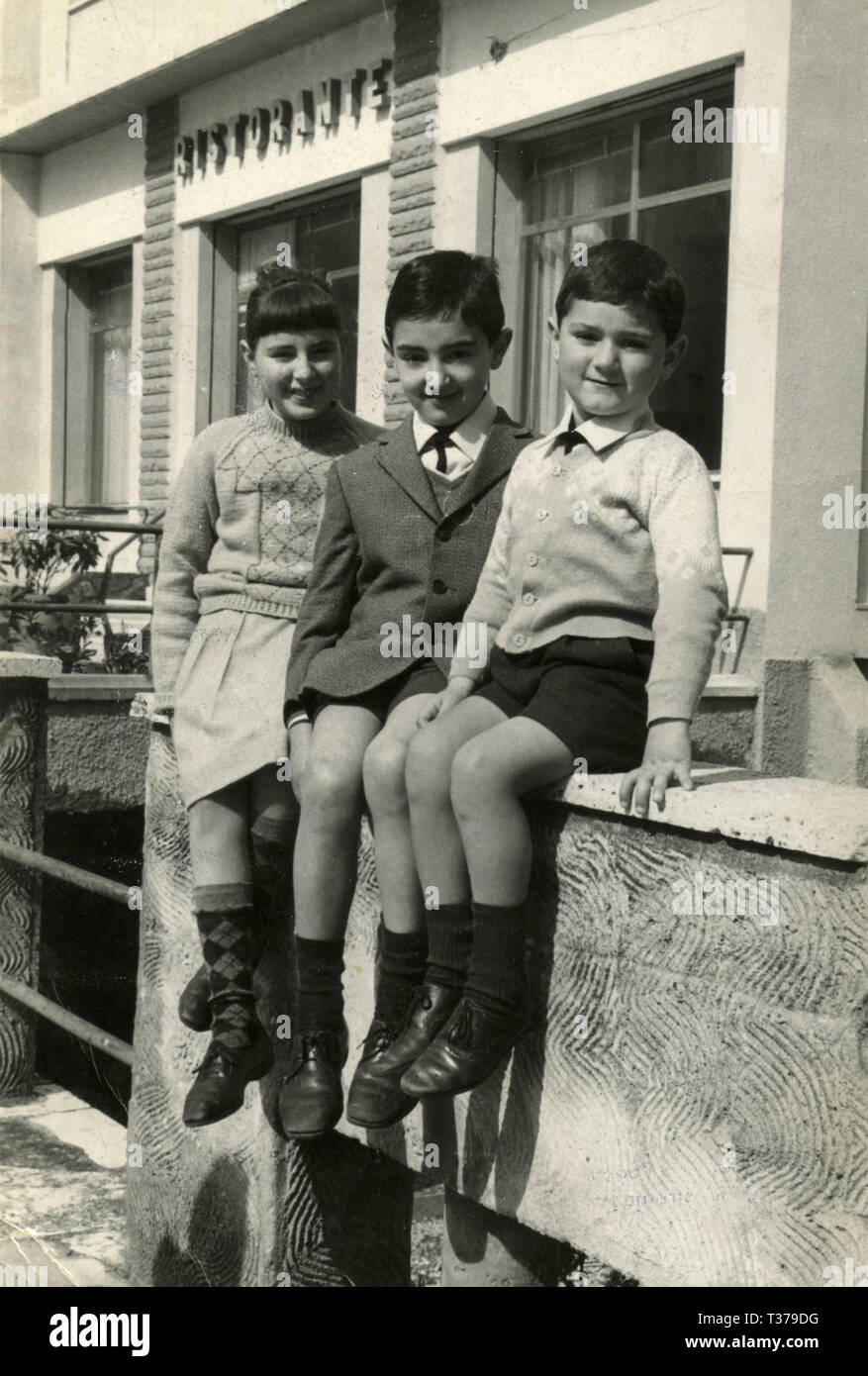 Two little men and a girl sitting on the wall, Italy 1960s Stock Photo ...