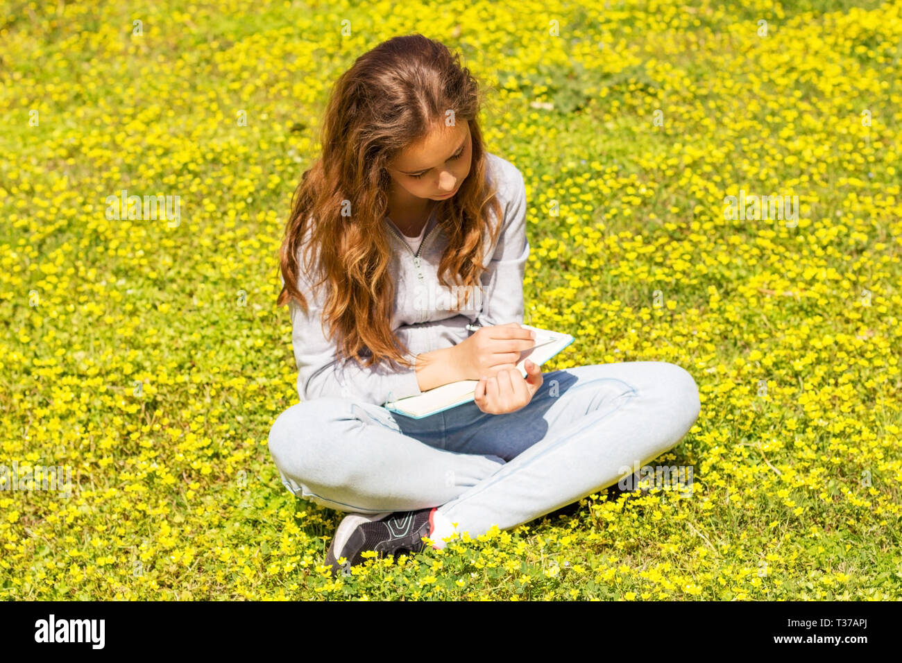Cute teen girl writes notes on a paper pad on green meadow Stock Photo ...
