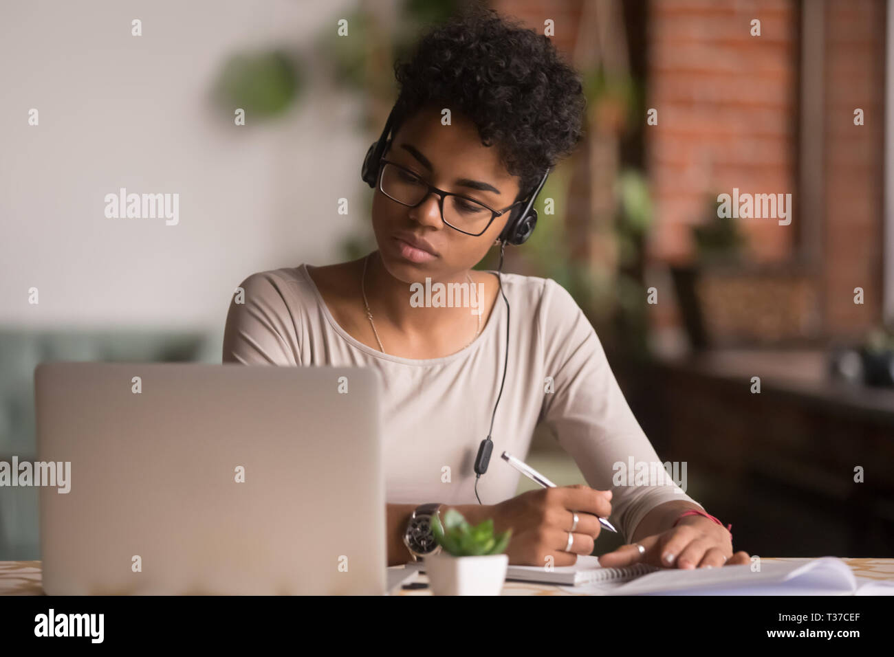 Focused mixed race woman wearing headphones watching webinar write ...