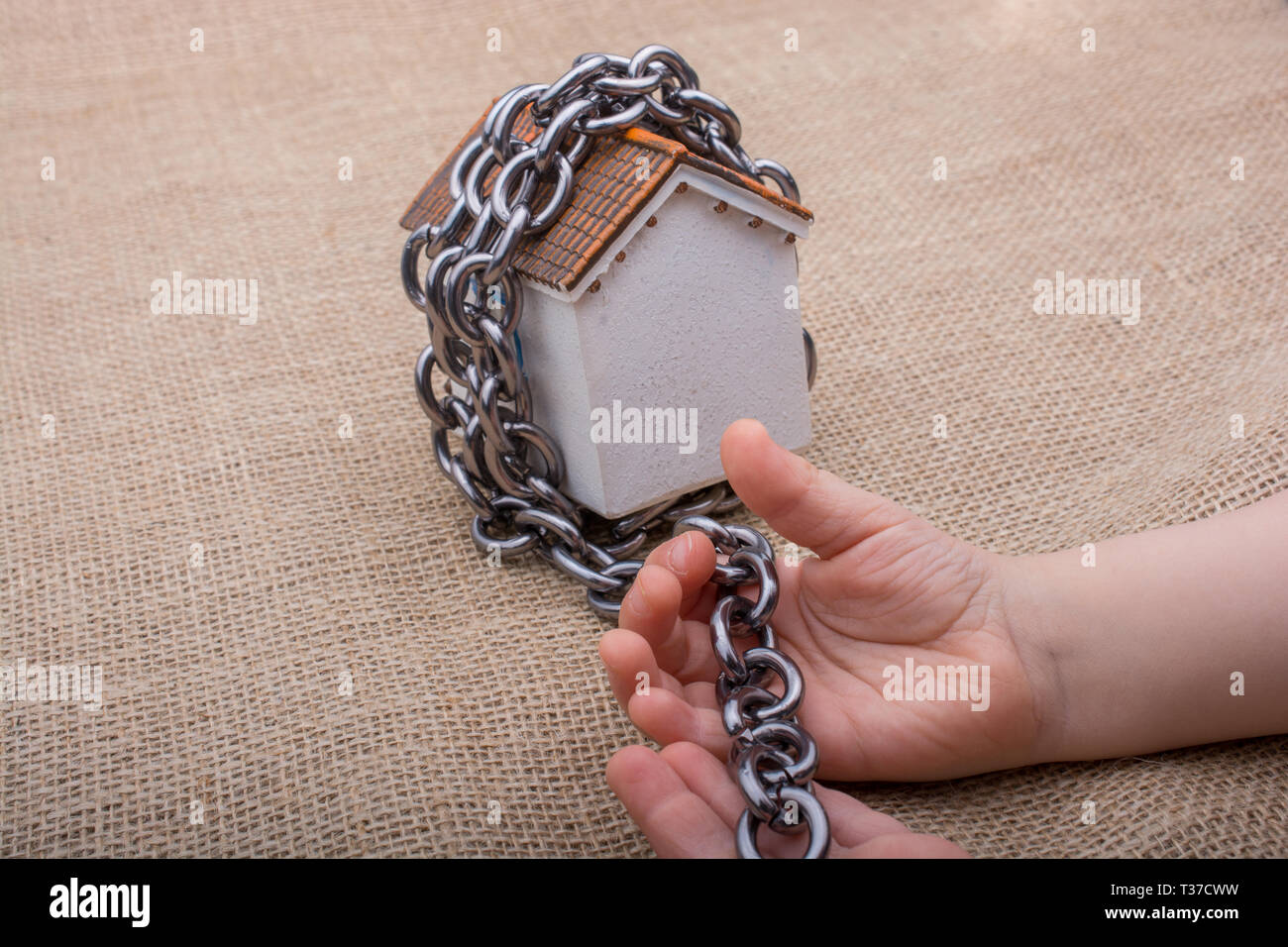 Little hand holding a chain around a model house on a brown background ...