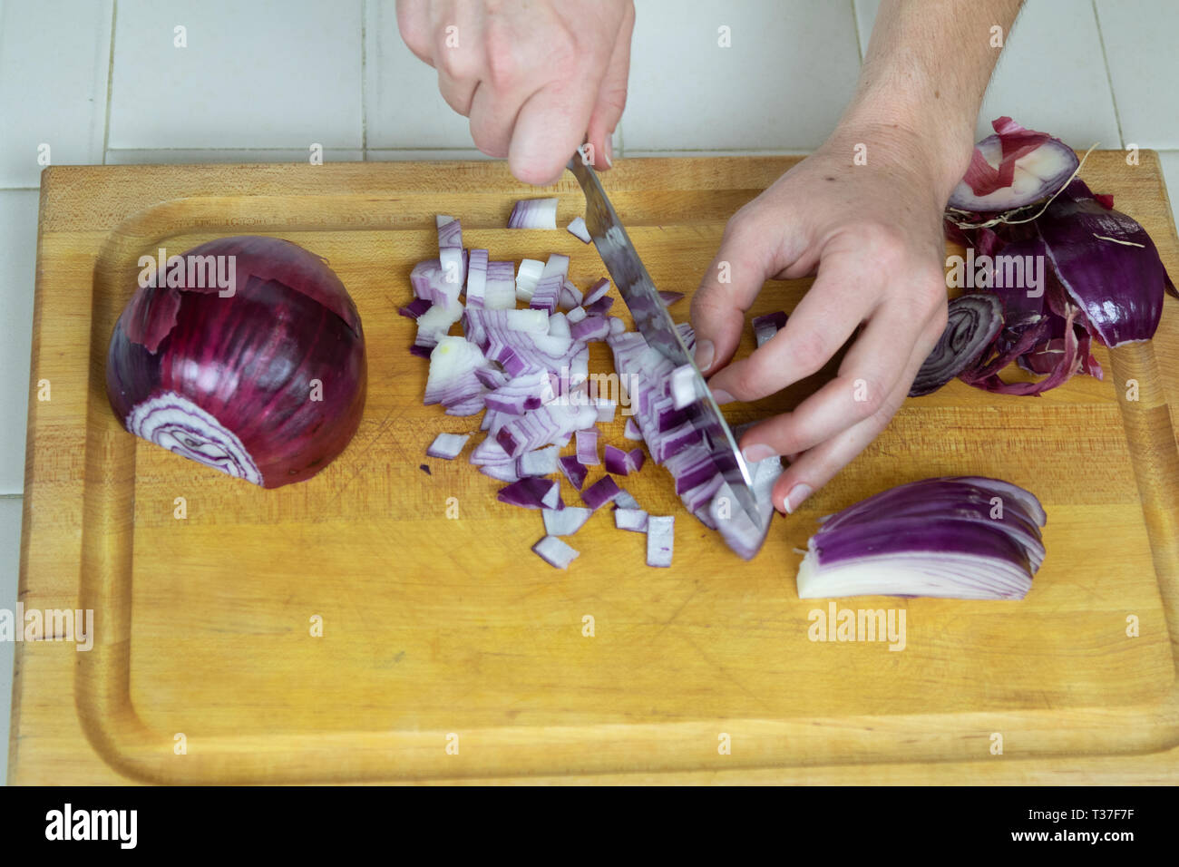 Overhead view of female hands dicing red onion slices with half the ...