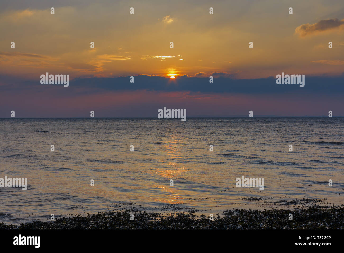 The sun about to disappear behind cloud-cover with a faint streak of ...