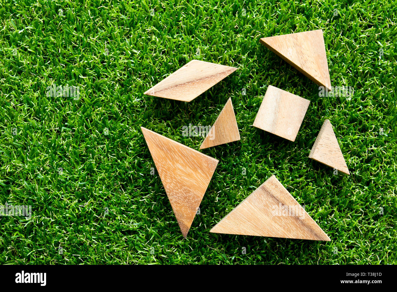Wooden tangram puzzle wait for complete on artificial green grass ...