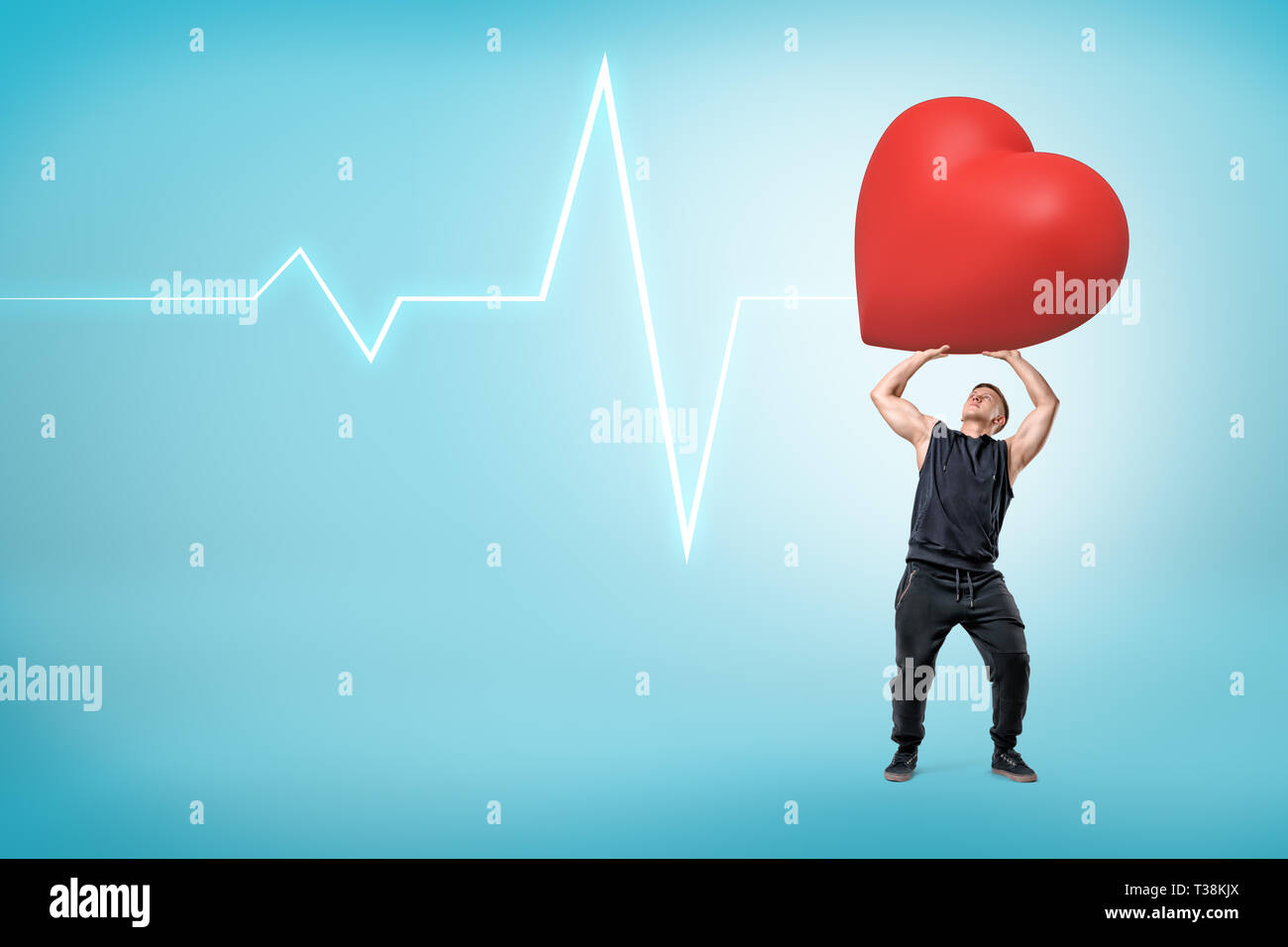 Man in sleeveless hoody holding up big heavy red heart on light-blue ...