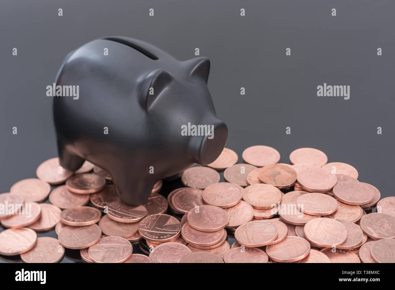 Black ceramic piggy bank with UK coins on reflective black background ...