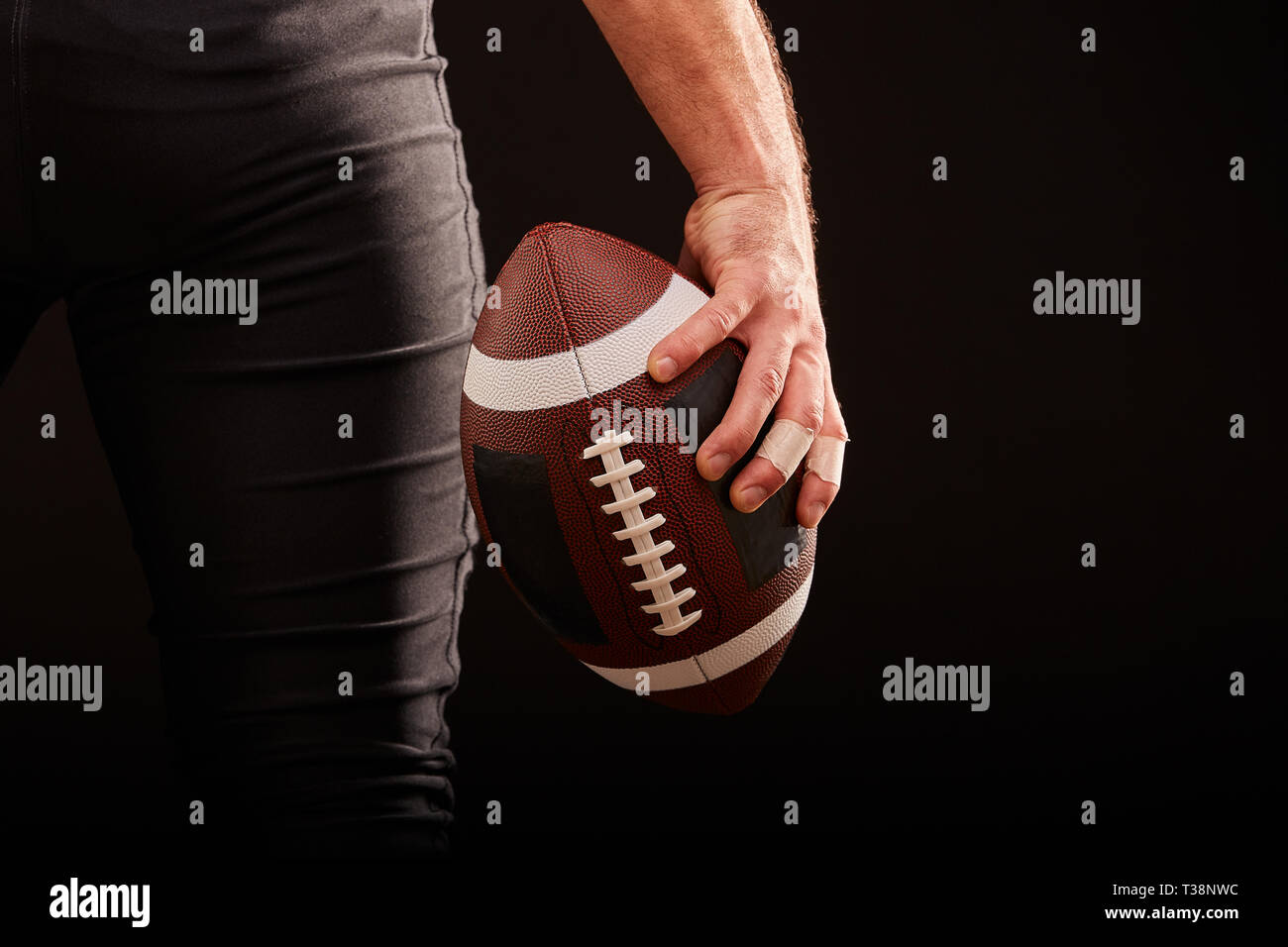 Mid section of American football player with ball against black, copy ...