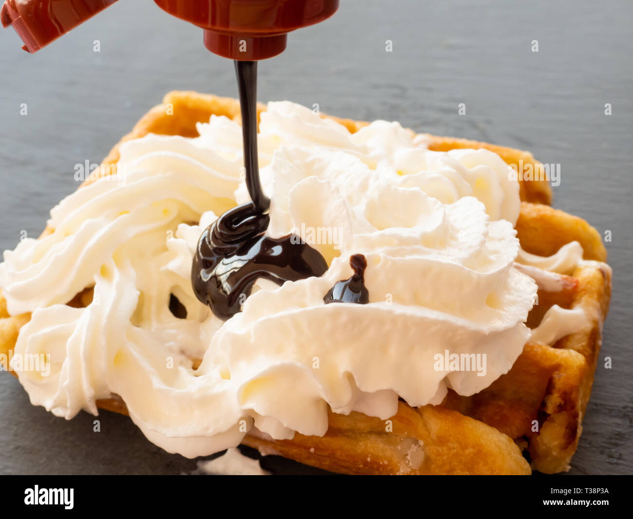 Chocolate syrup falling on a Belgian waffle with cream on a slate plate ...