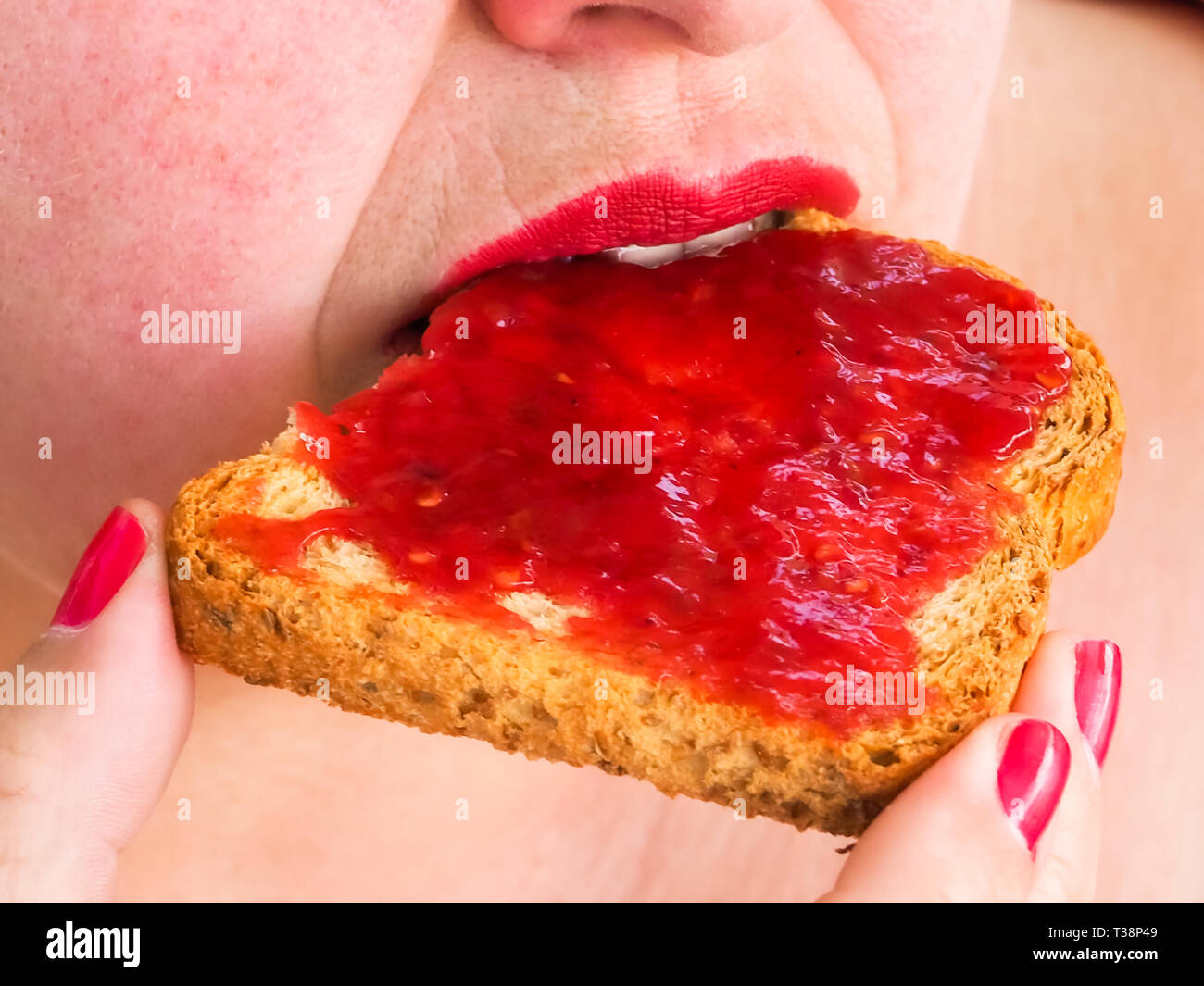 An adult woman with red nails and lips eating a rusk with raspberry jam ...