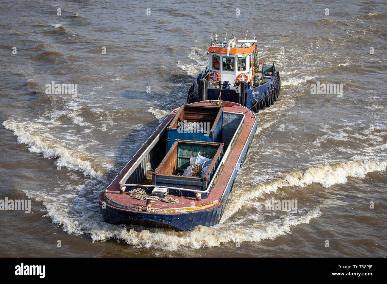 Looking down at a tugboat pushing a large cargo barge carrying waste ...