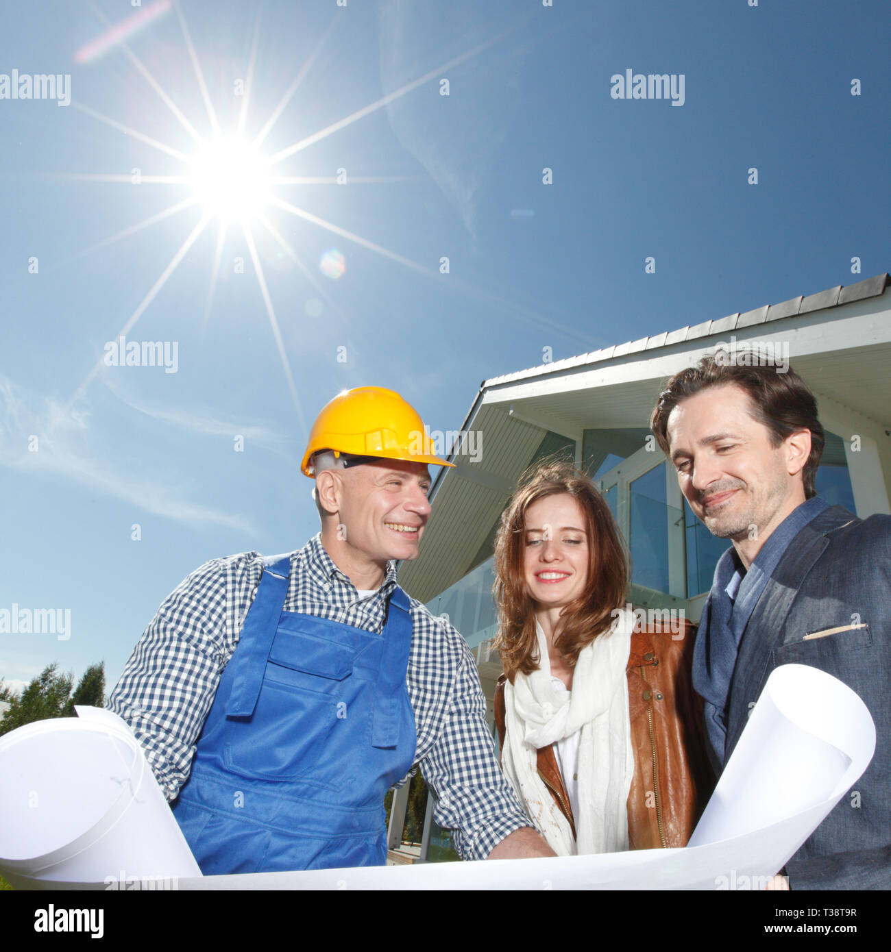 Worker shows house design plans to a young couple at construction site ...