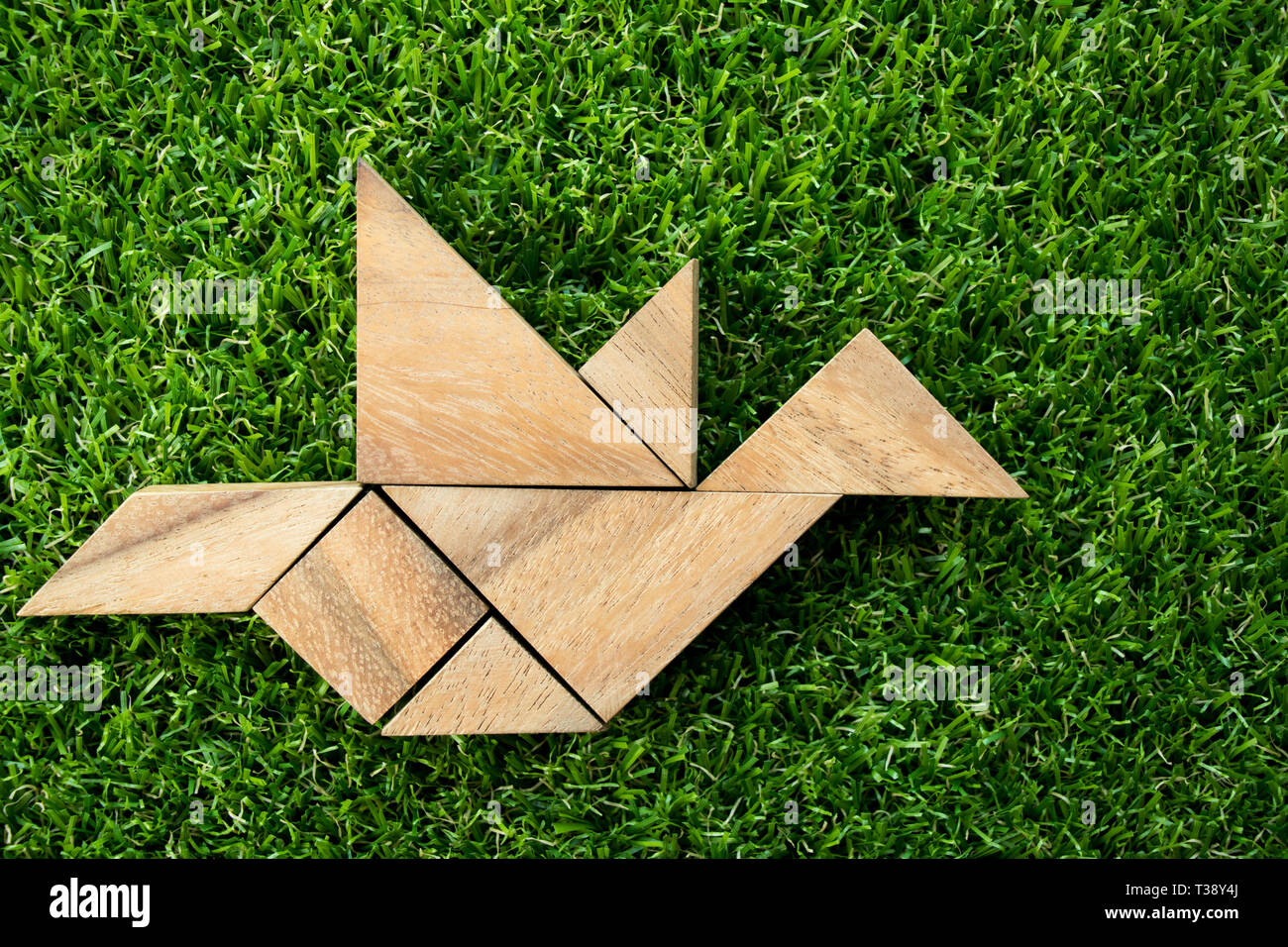 Wooden tangram puzzle in flying bird shape on artificial green grass ...