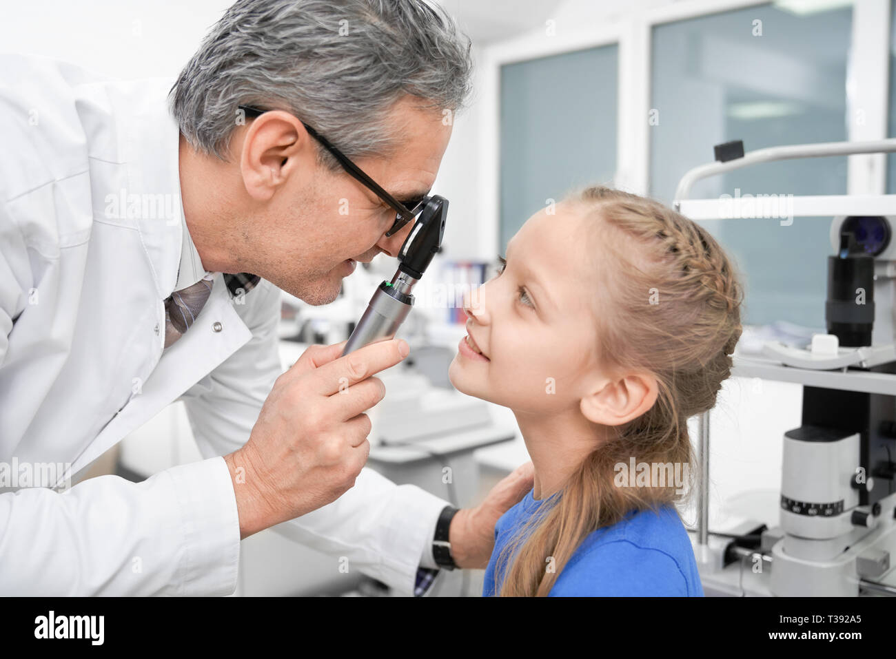 View from side of male oculist checking sight of girl in clinic. Elder ...