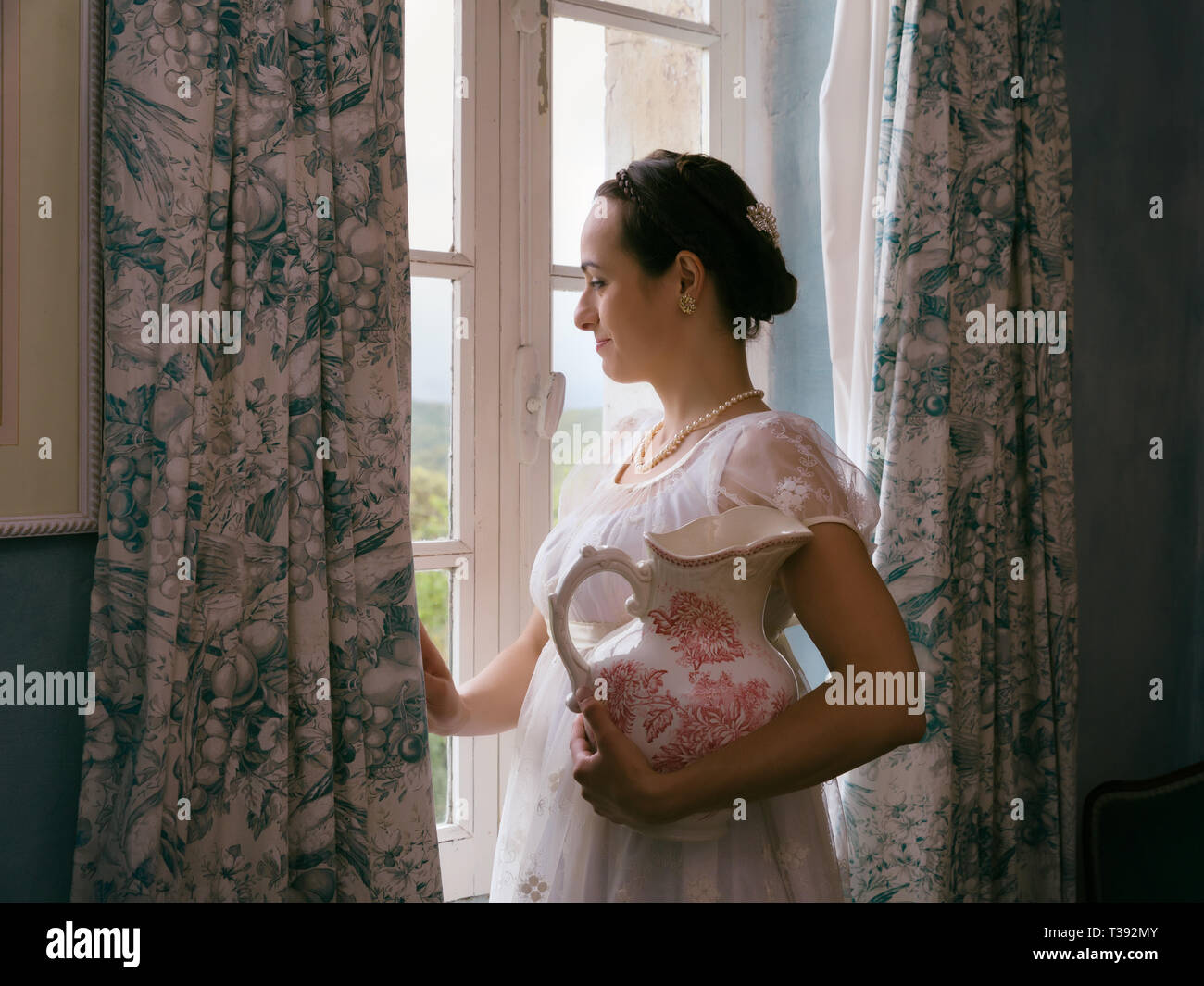 Young woman in authentic regency dress near a window of a classical ...